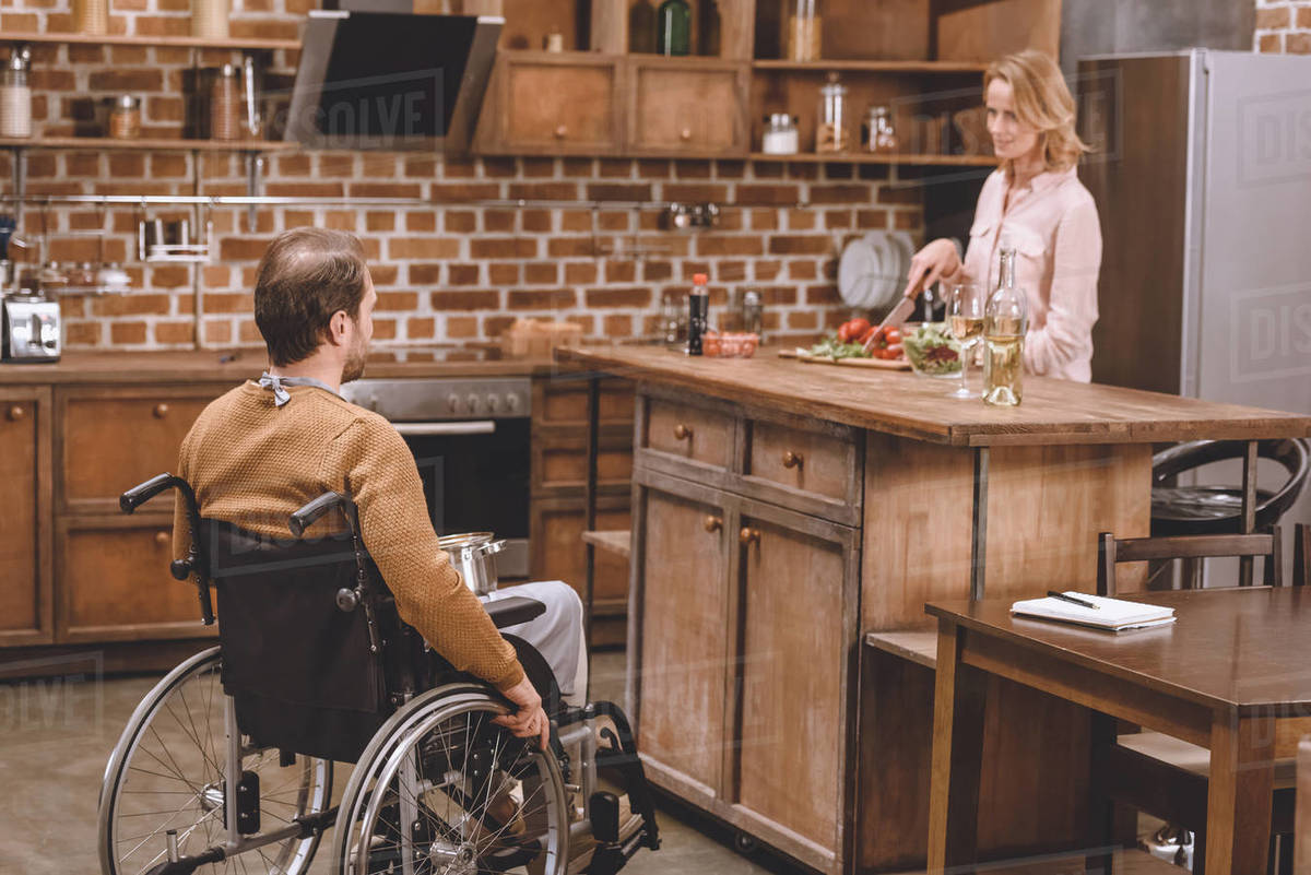 woman with disabled man in wheelchair cooking dinner together at home ...