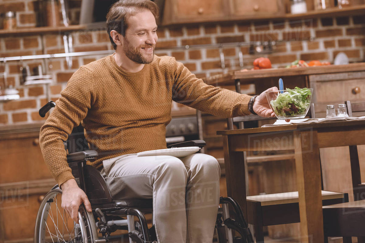 smiling disabled man in wheelchair holding glass bowl of vegetable ...