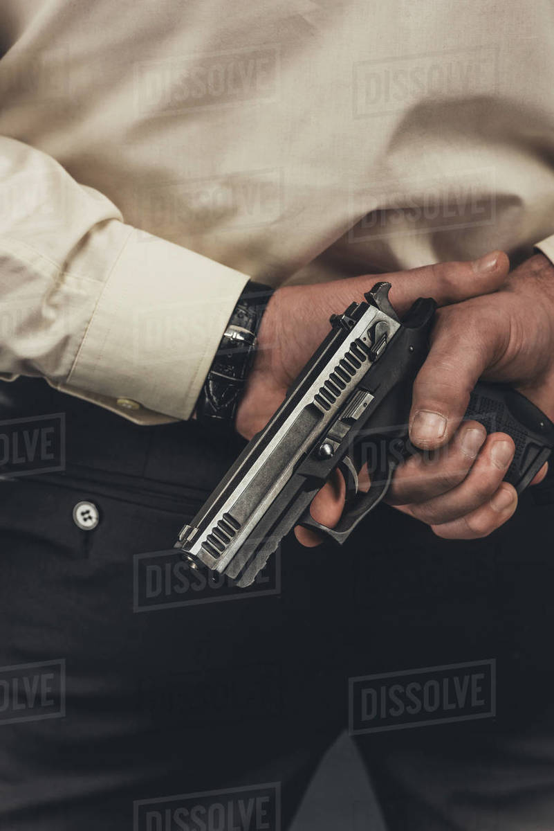 Cropped shot of man in shirt holding gun behind back - Royalty-free ...