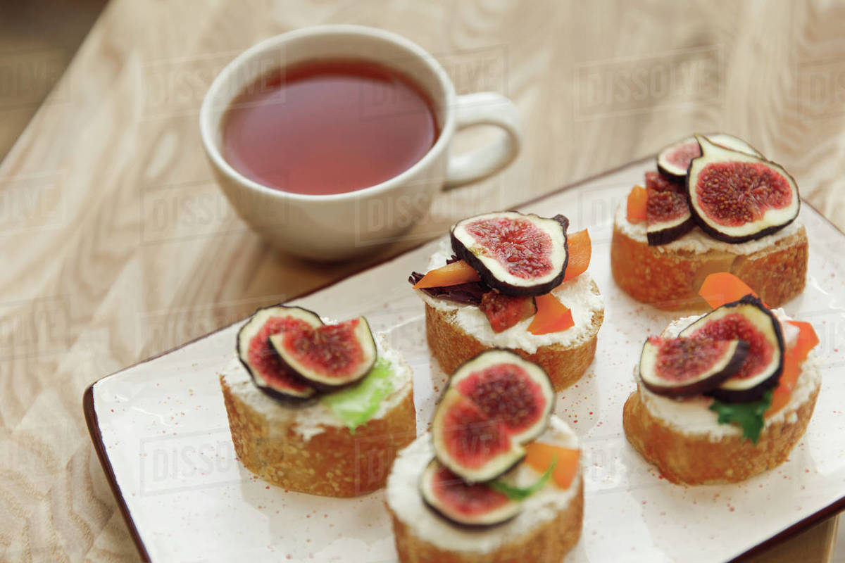 Close-up view of canapes with figs and cup of tea on table - Royalty ...