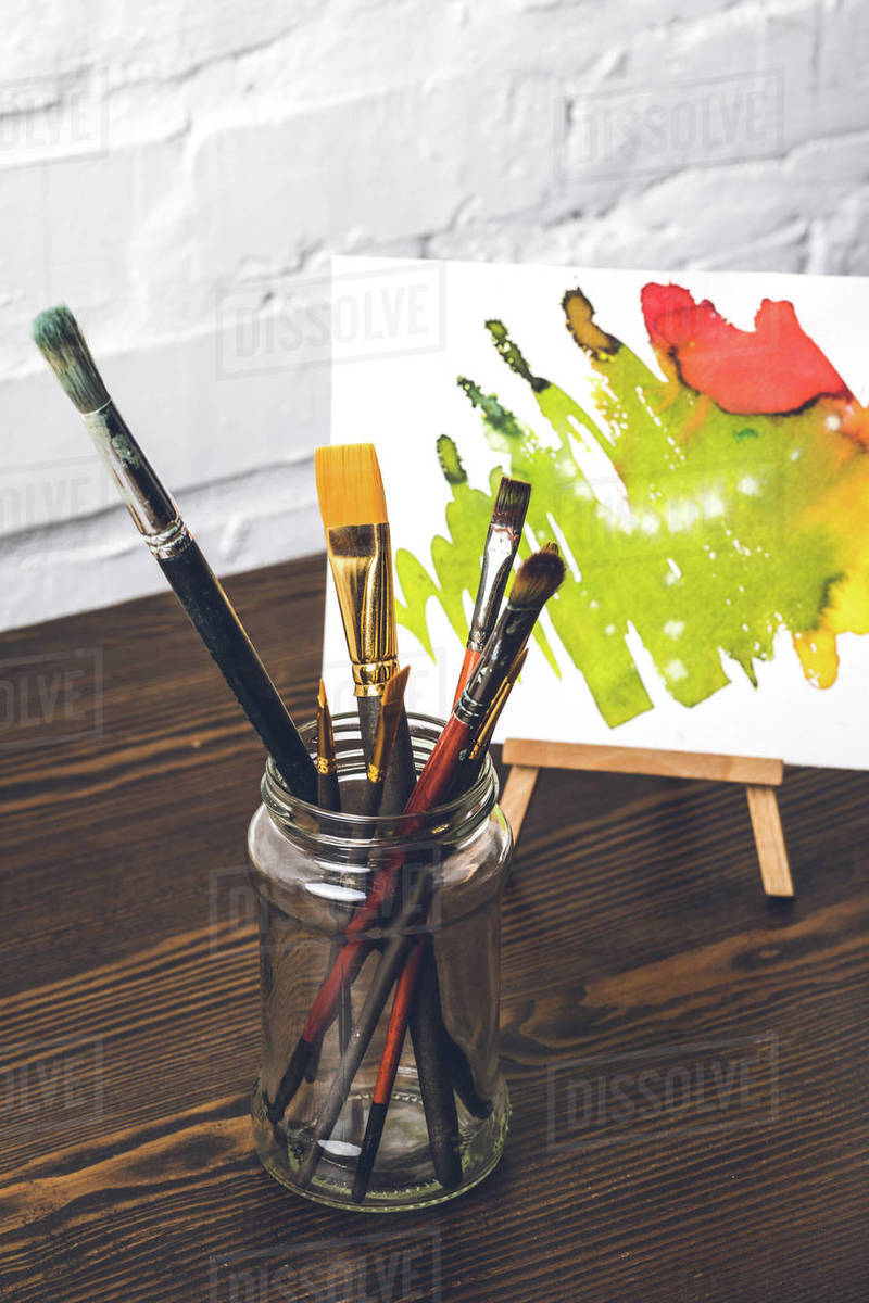 Close-up view of various paint brushes in glass and abstract painting ...