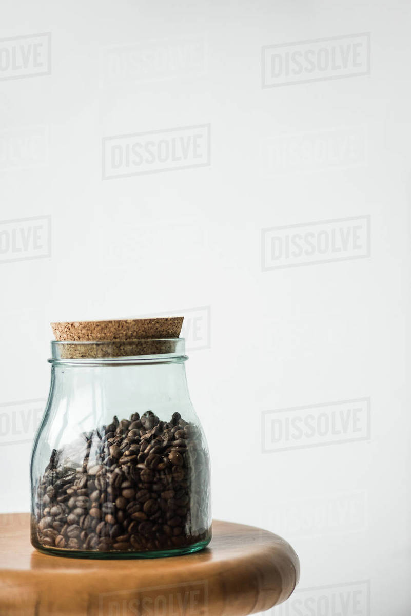 Glass bottle with coffee beans and cap on wooden stand isolated on ...
