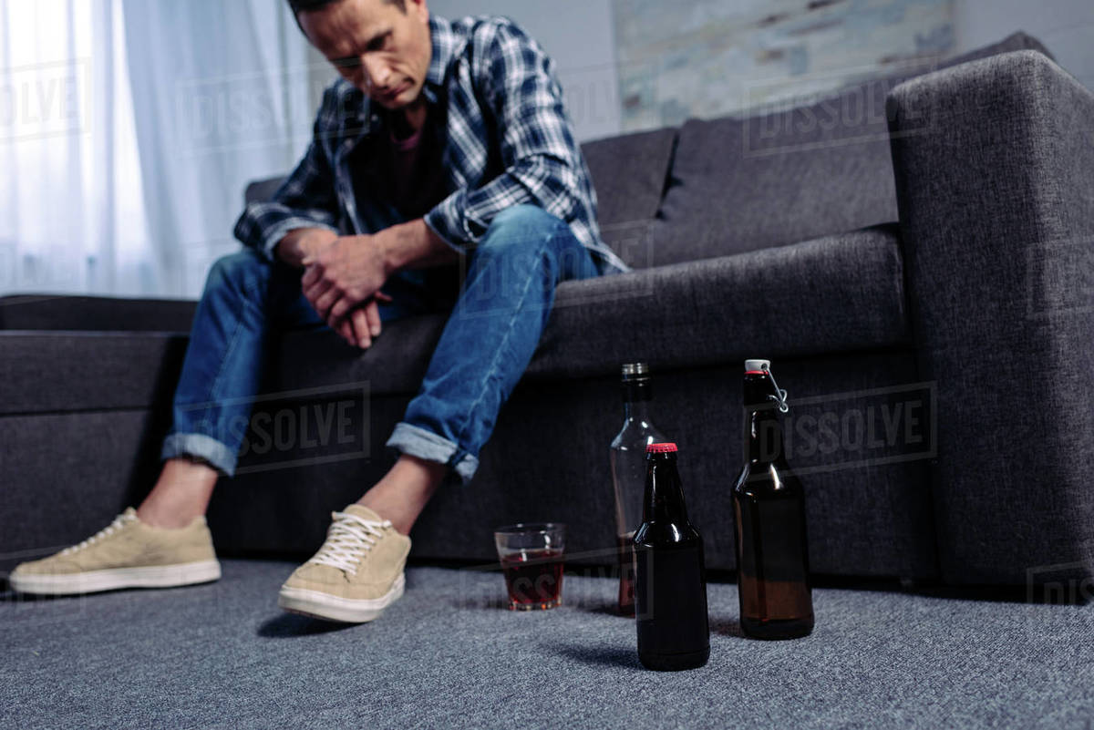 Man looking at alcohol on floor while sitting on sofa at home - Royalty ...