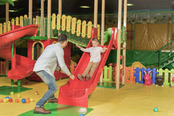 father with adorable little son playing on slide at indoor play center ...