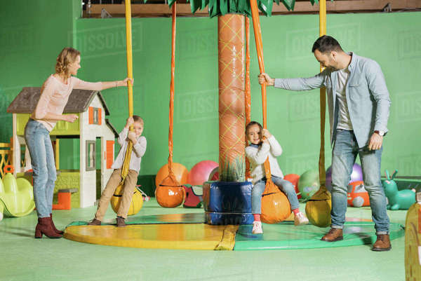 smiling parents looking at cute happy children swinging on swings in ...