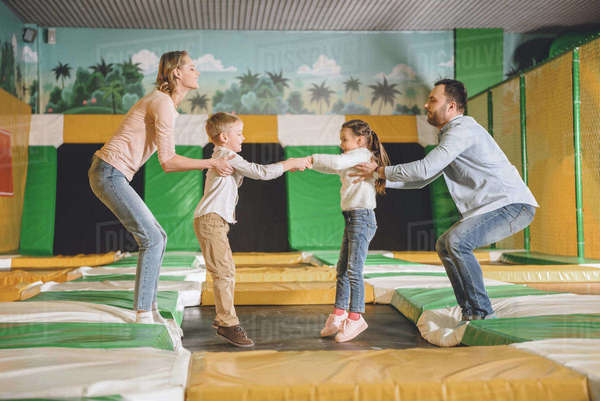 side view of happy family with two kids playing together in game center ...