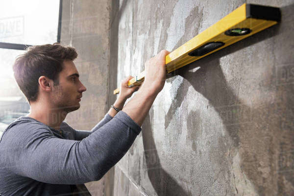 Professional young worker measuring wall with level tool, renovation ...