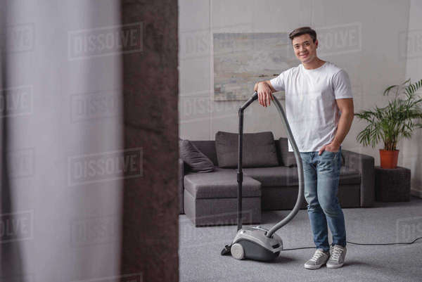 Handsome man leaning on vacuum cleaner in living room - Royalty-free ...