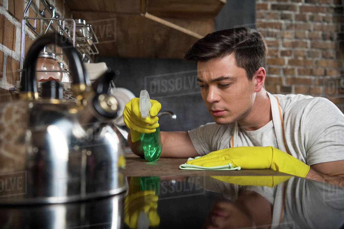 Serious handsome man cleaning kitchen with spray bottle and rag ...