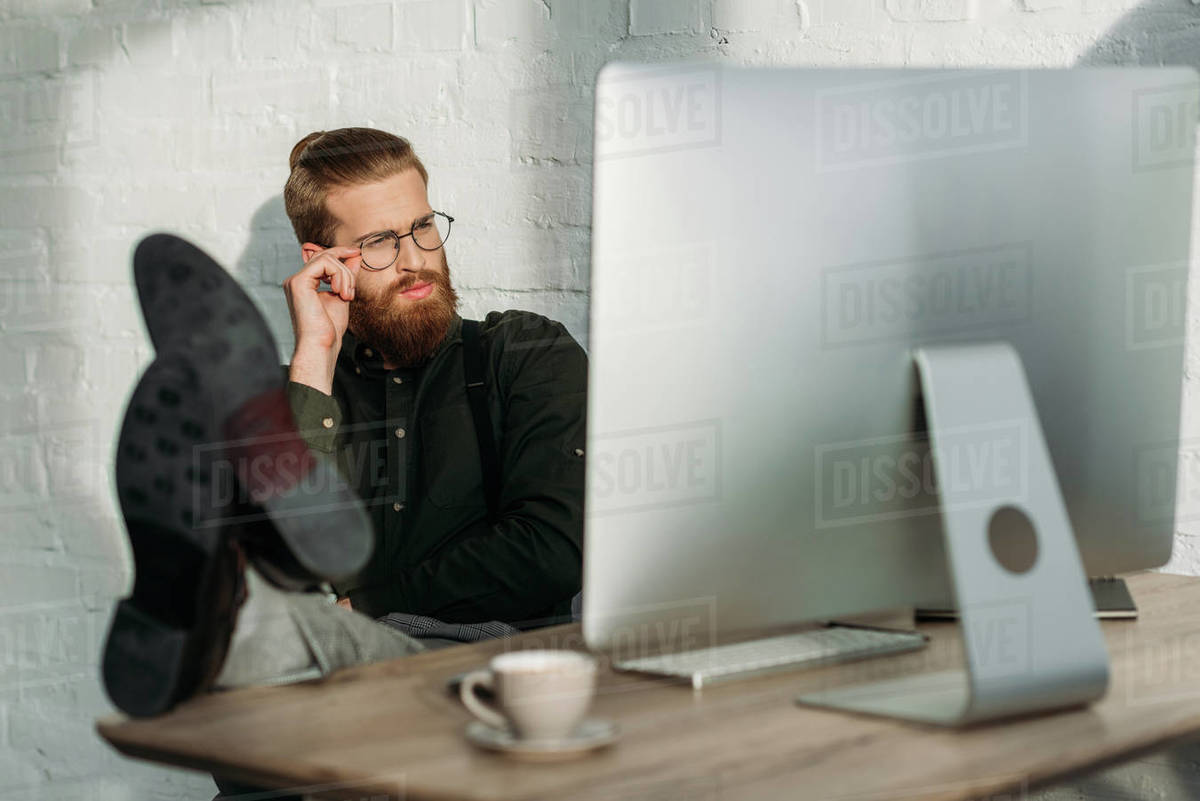 Businessman sitting with legs on office table and looking at computer ...