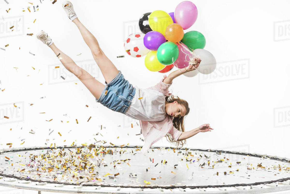 Girl holding colorful balloons and falling on trampoline isolated on ...