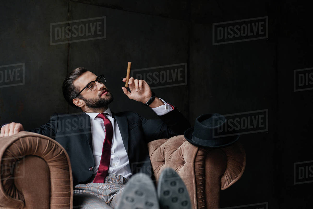 Handsome stylish businessman with cigar posing in armchair - Royalty ...