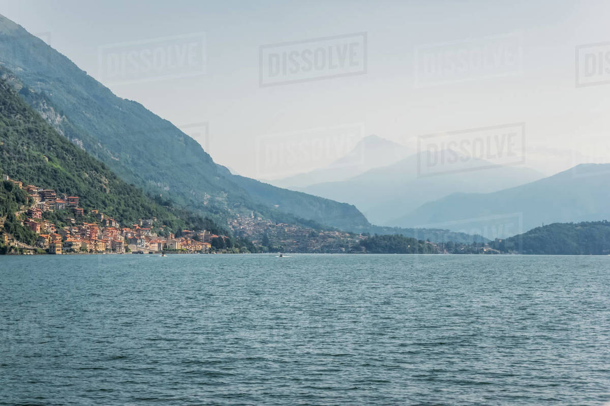 View of mountain lake and hills on shore with buildings during daytime ...