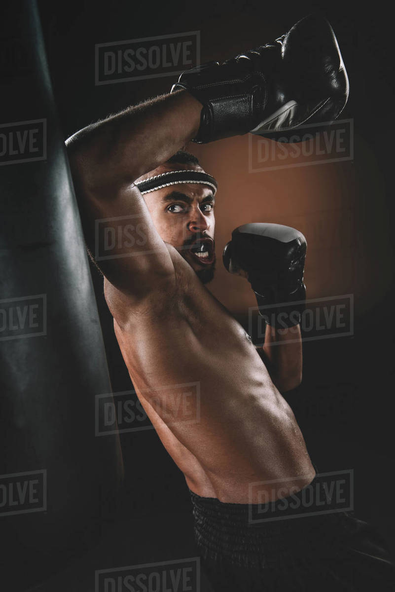 Aggressive young muay thai fighter in boxing gloves training thai ...