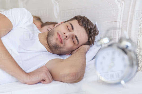 Handsome young man sleeping in morning with blurred alarm clock on ...