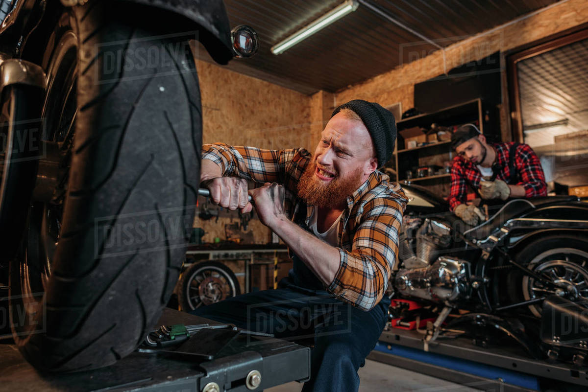 Tensed mechanic fixing motorcycle while his colleague working on ...