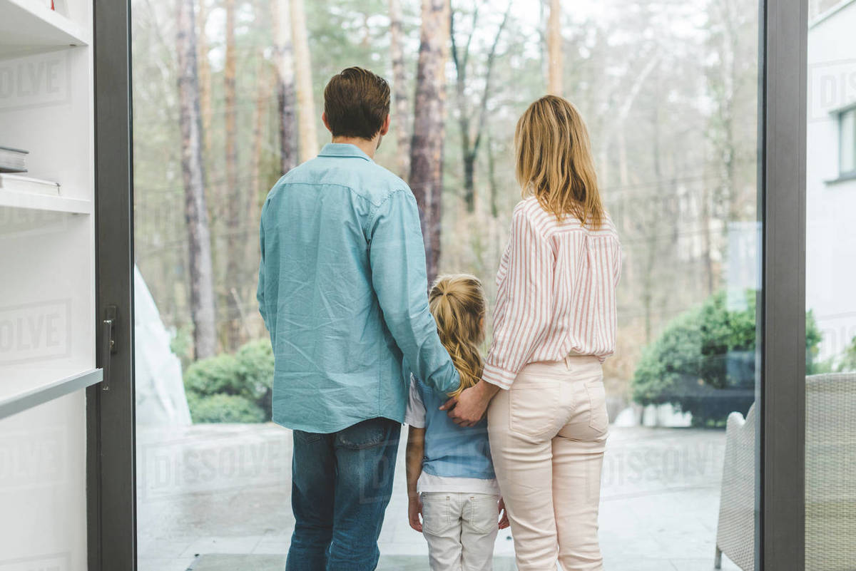 Back view of family looking out window at home - Stock Photo - Dissolve