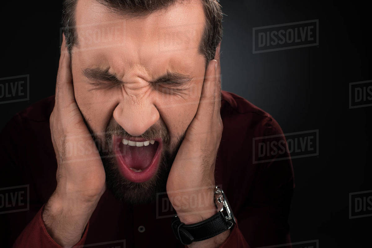 Portrait of screaming man covering ears isolated on black - Royalty ...