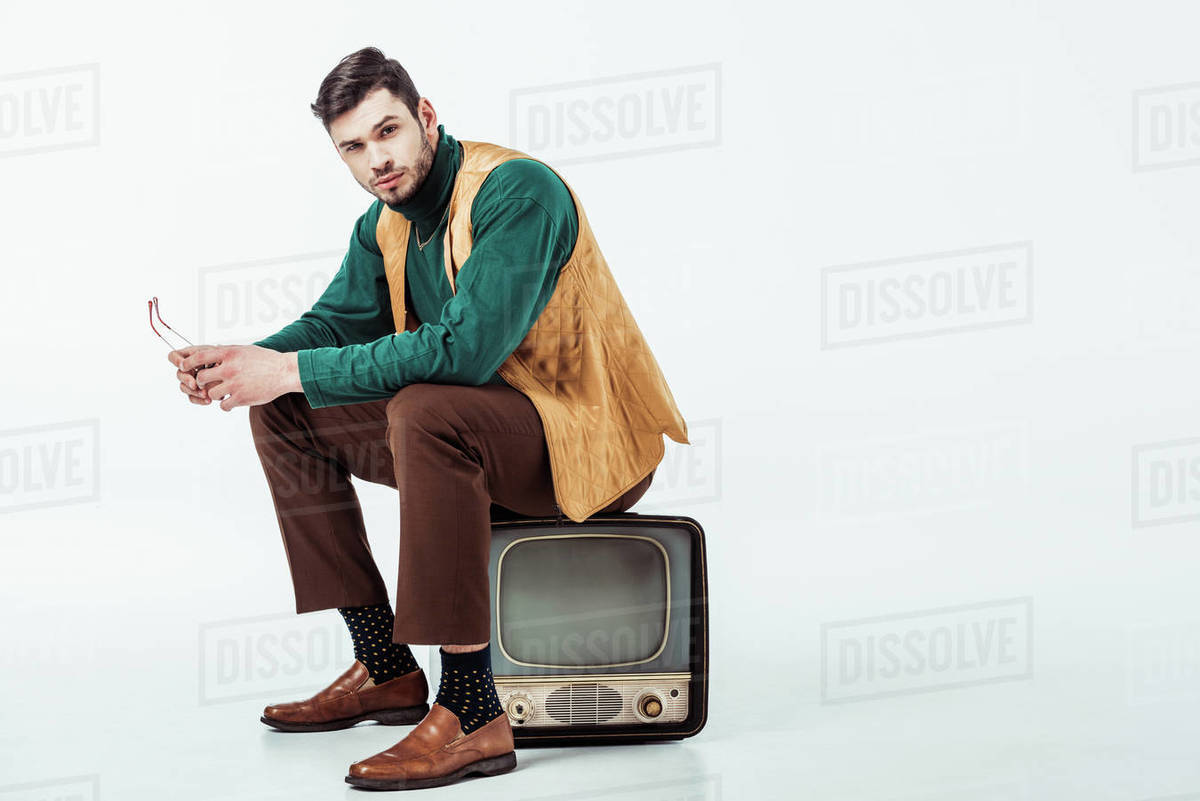 Handsome retro styled man sitting on vintage television and looking at ...