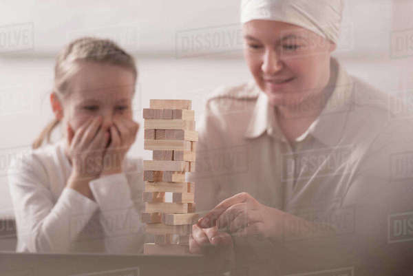 Child with sick grandmother in kerchief playing with wooden blocks ...