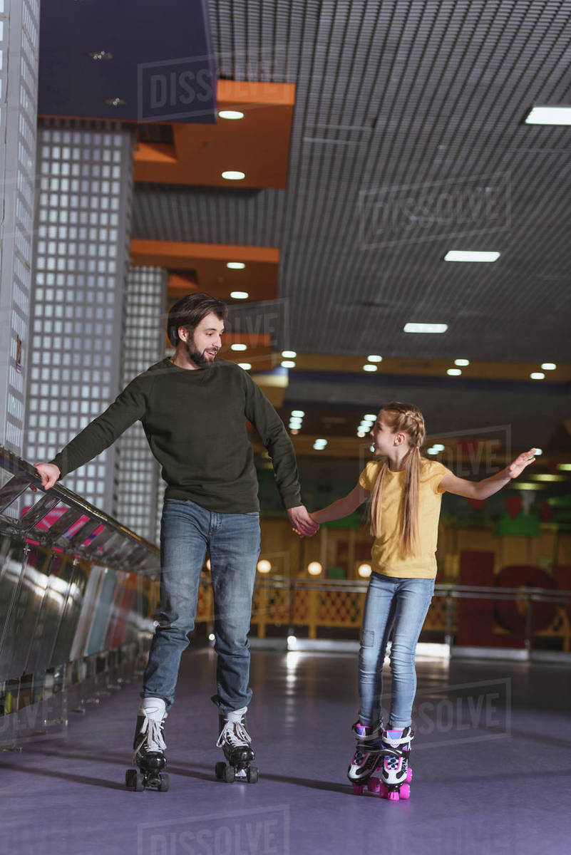 Father and daughter holding hands while skating together on roller rink ...