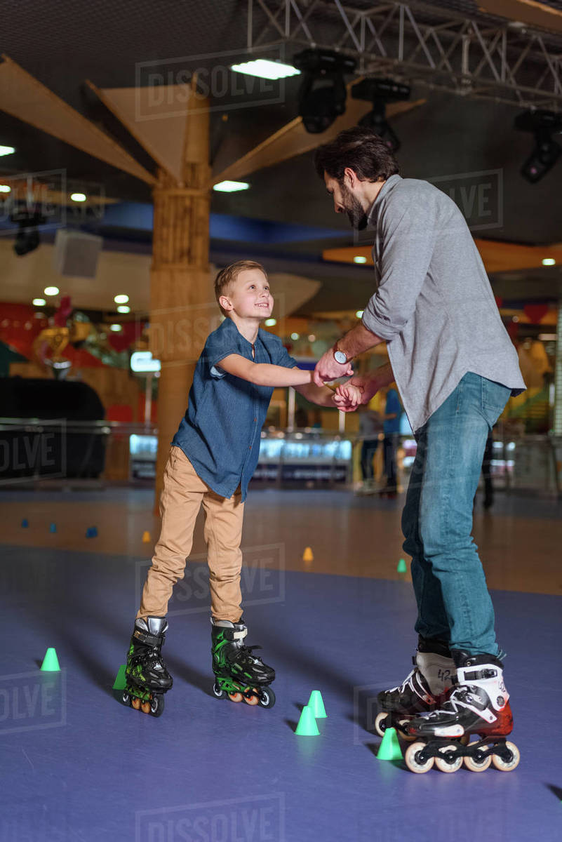 Father and son skating together on roller rink with cones - Royalty ...
