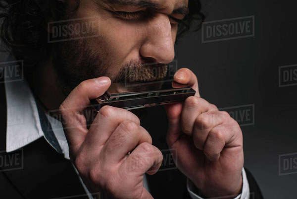 Close-up portrait of expressive musician playing harmonica on black ...