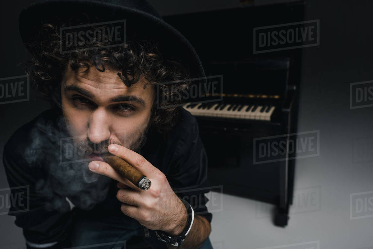 Close-up portrait of young musician smoking cigar in front of piano and ...