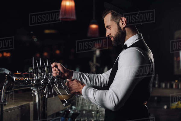 Side view of bartender pouring beer from beer taps into glass - Royalty ...