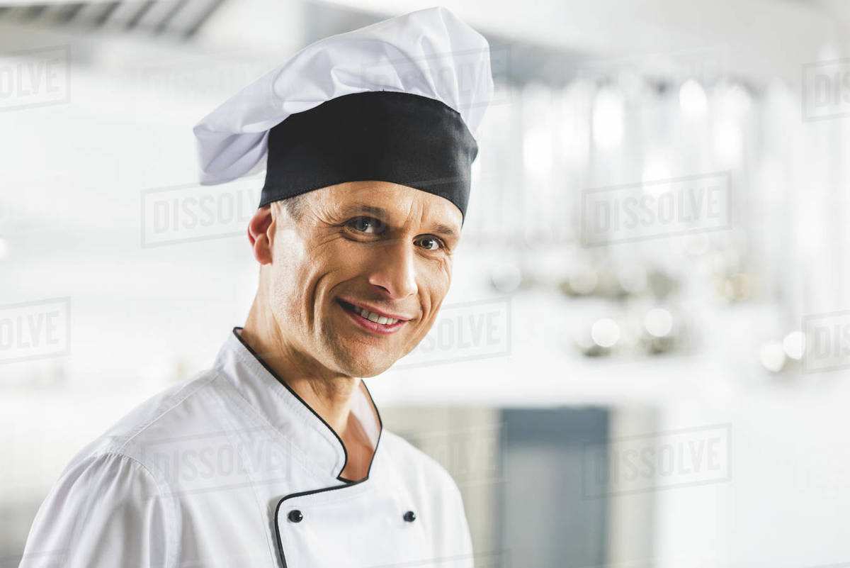 Portrait of smiling handsome chef looking at camera at restaurant ...