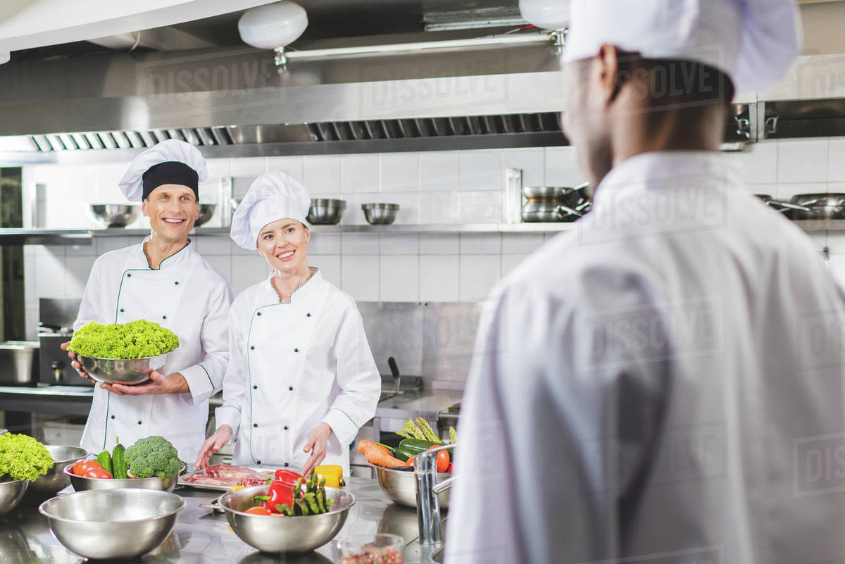 Smiling multicultural chefs looking at each other at restaurant kitchen ...