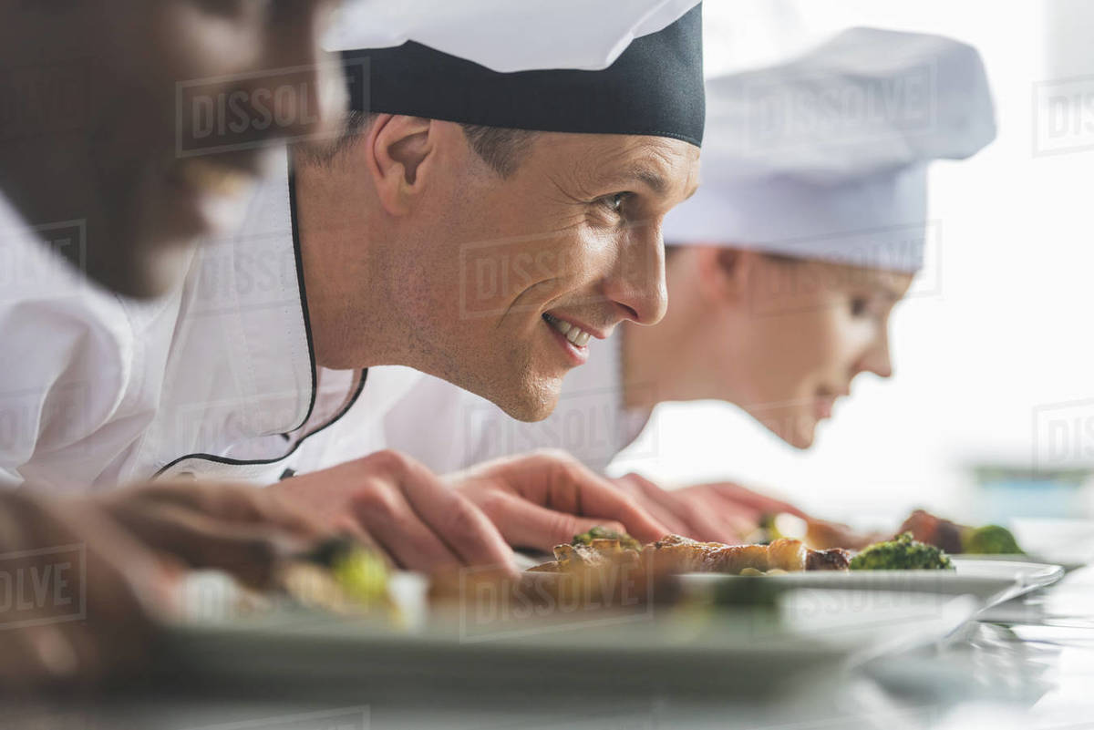 Smiling multiethnic chefs sniffing cooked food at restaurant kitchen ...