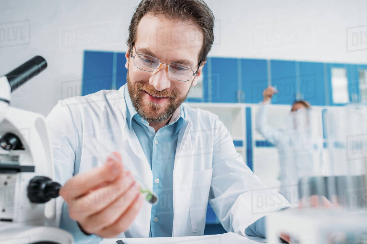 selective focus of smiling scientist in white coat and eyeglasses ...