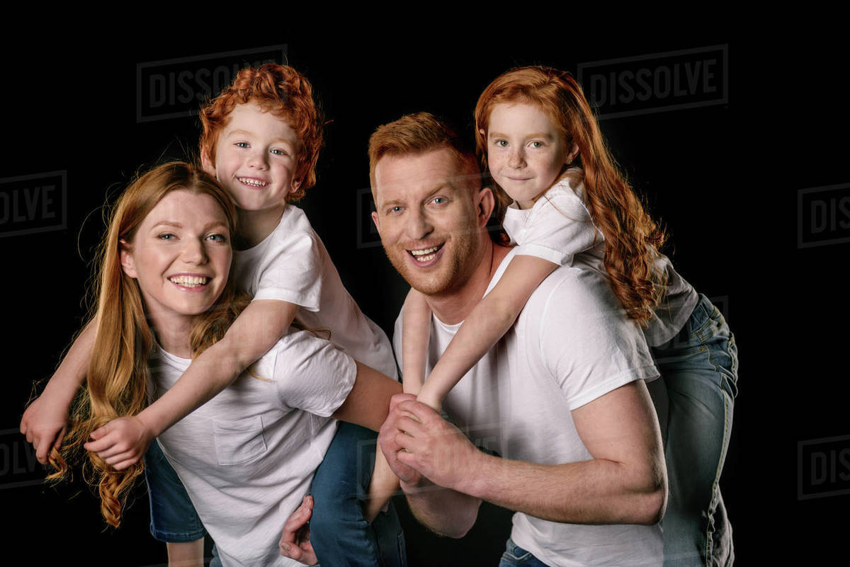 Happy redhead family in white t-shirts smiling isolated on black ...