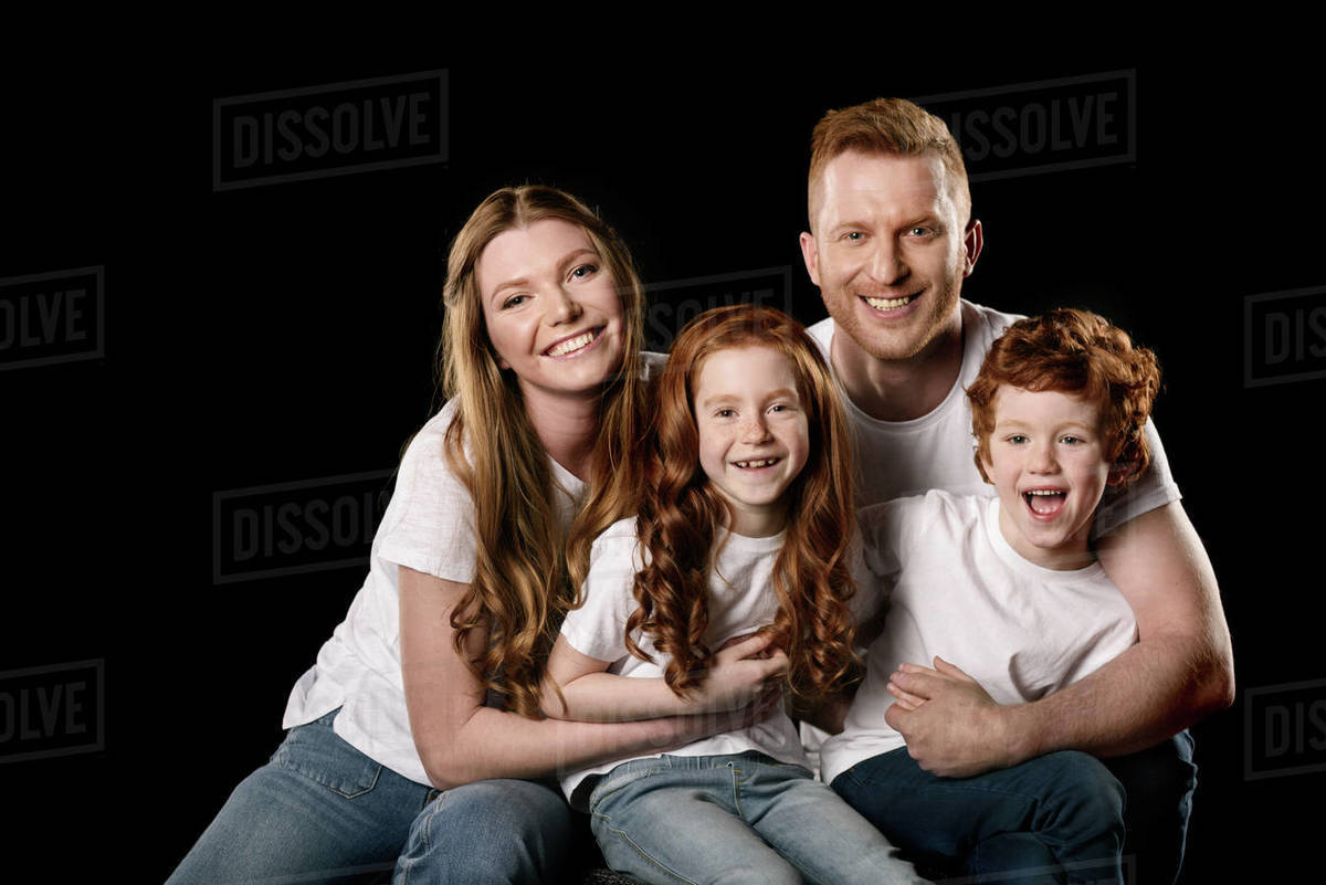 Happy redhead family sitting embracing and smiling at camera isolated ...