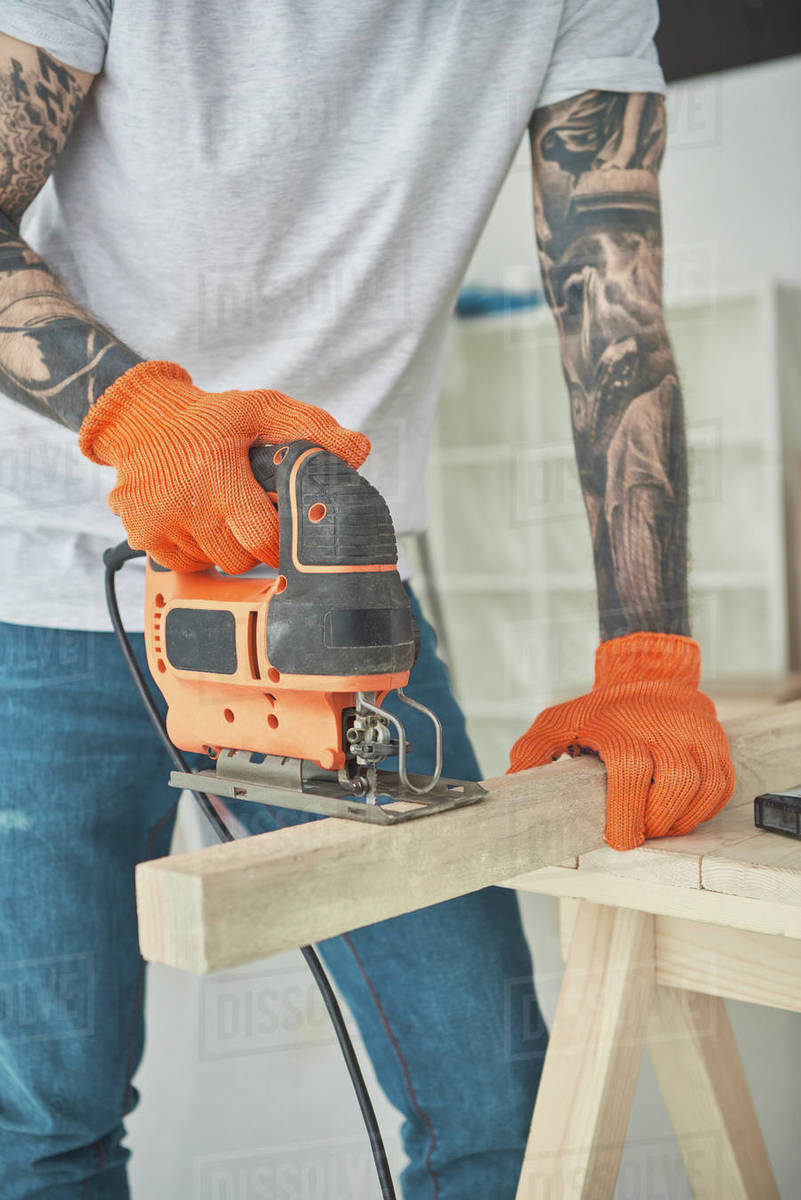 Cropped shot of young tattooed man using electric jigsaw - Royalty-free ...