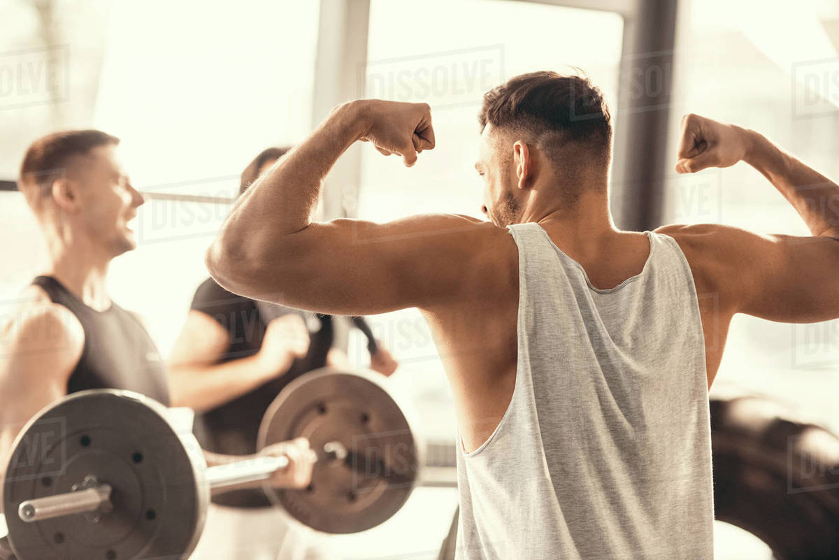 Back view of young sportsman showing muscles to friends in gym - Stock ...