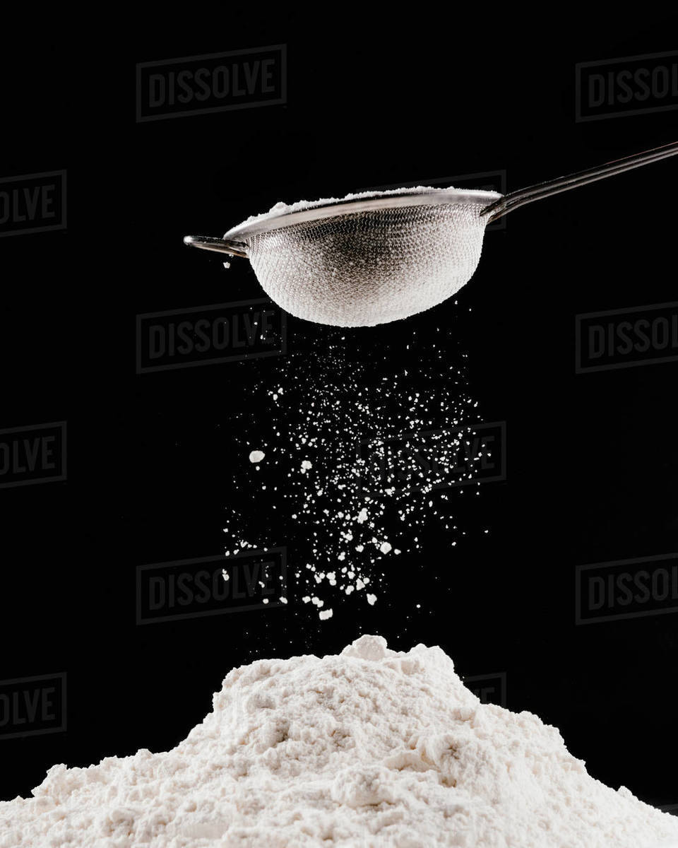 Flour falling from sieve on pile for pastry isolated on black - Royalty ...