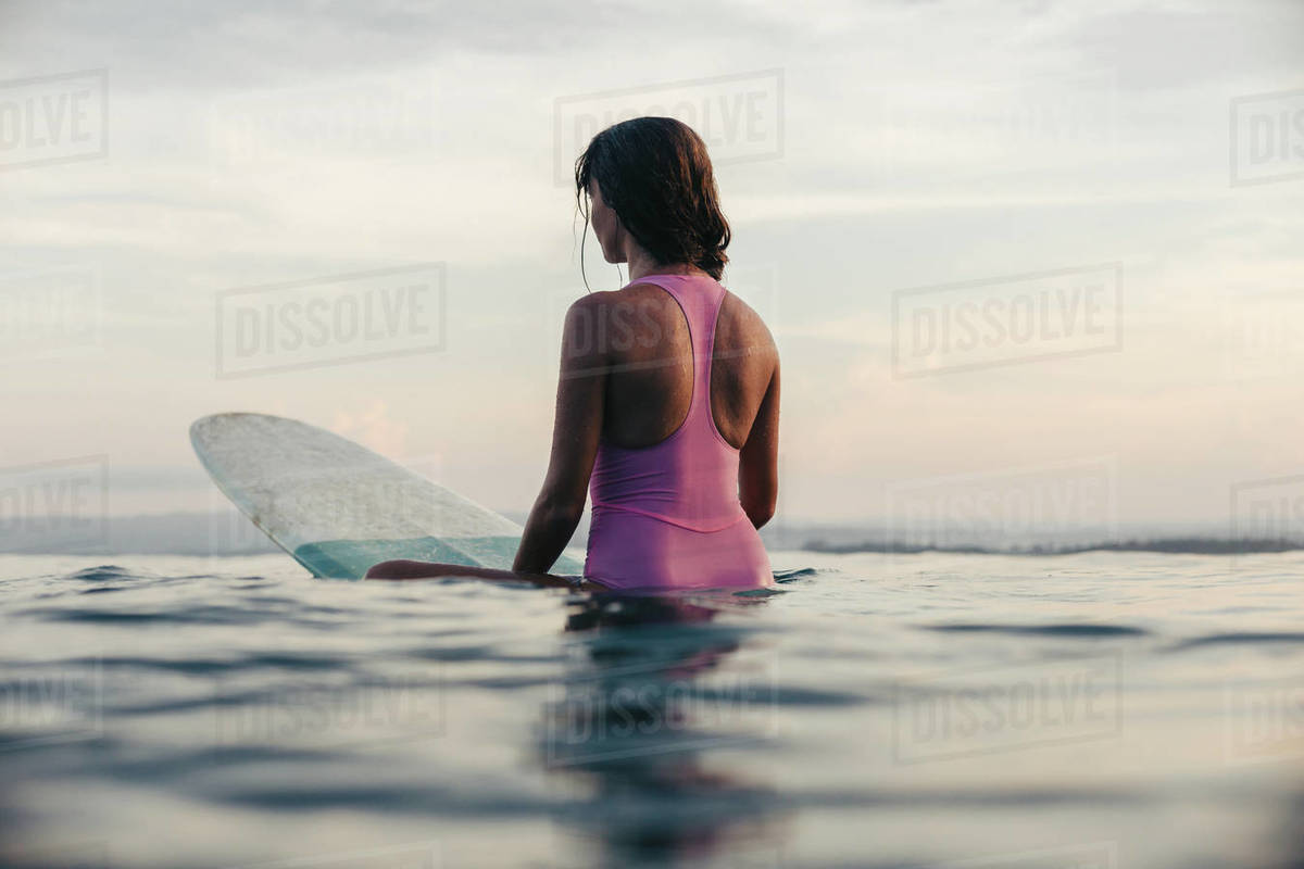 Back view of girl sitting on surfboard in ocean at sunset - Royalty ...