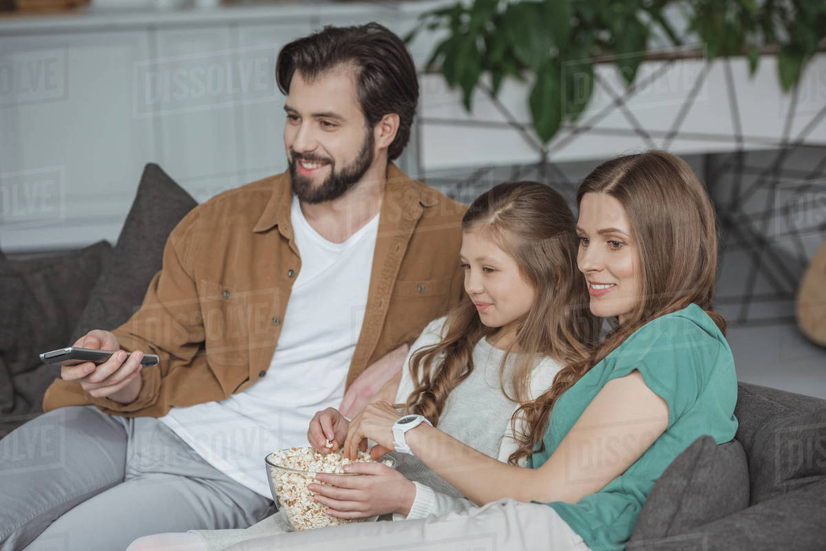 Happy parents and daughter watching tv with popcorn at home - Royalty ...