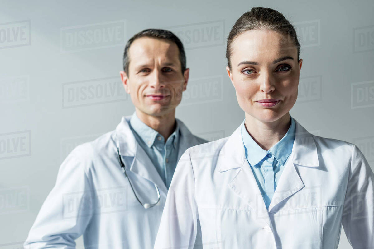 Close-up portrait of attractive adult doctors looking at camera on grey ...