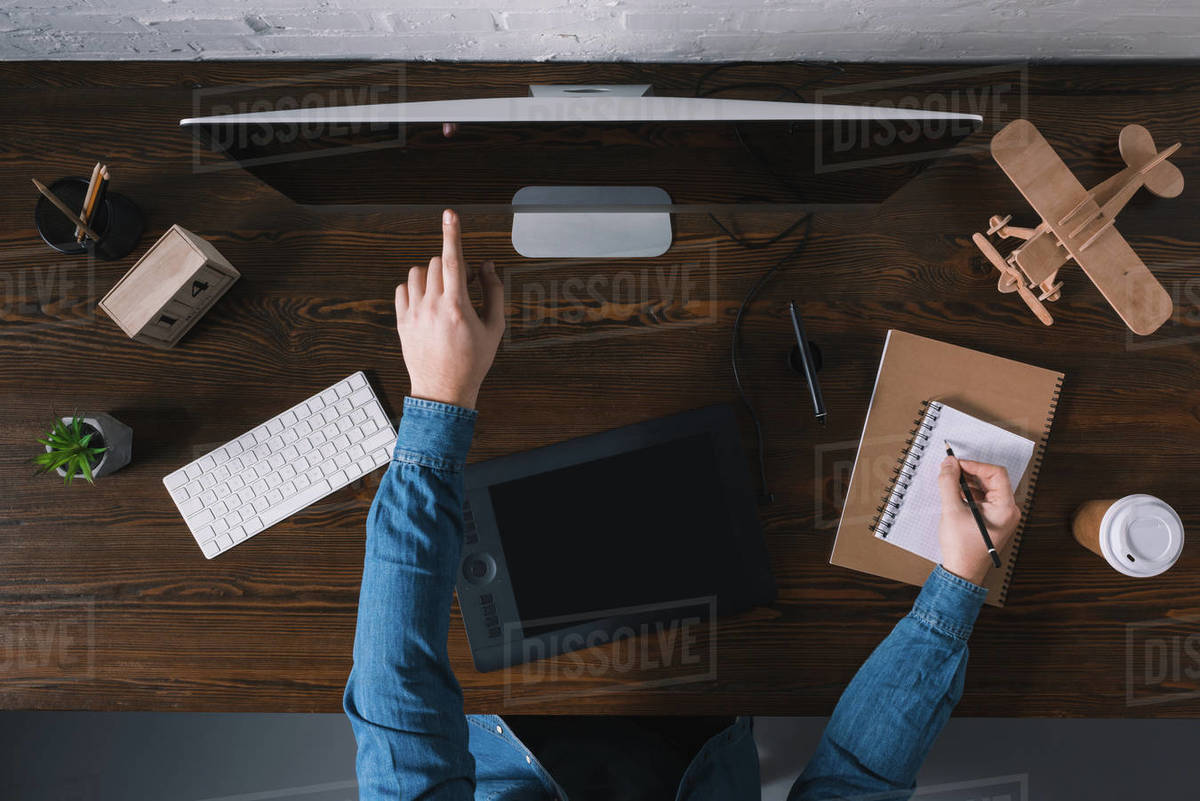 Cropped shot of person using desktop computer and taking notes at ...