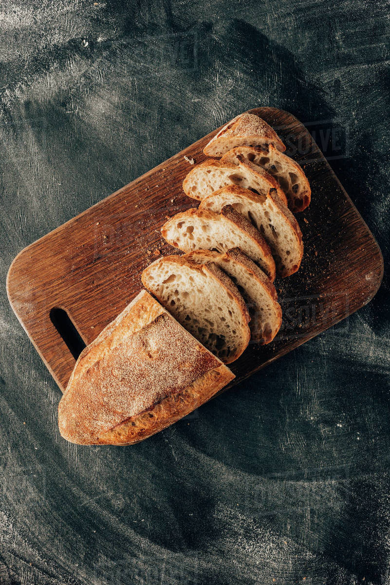 Top view of arranged pieces of bread on cutting board on dark surface ...
