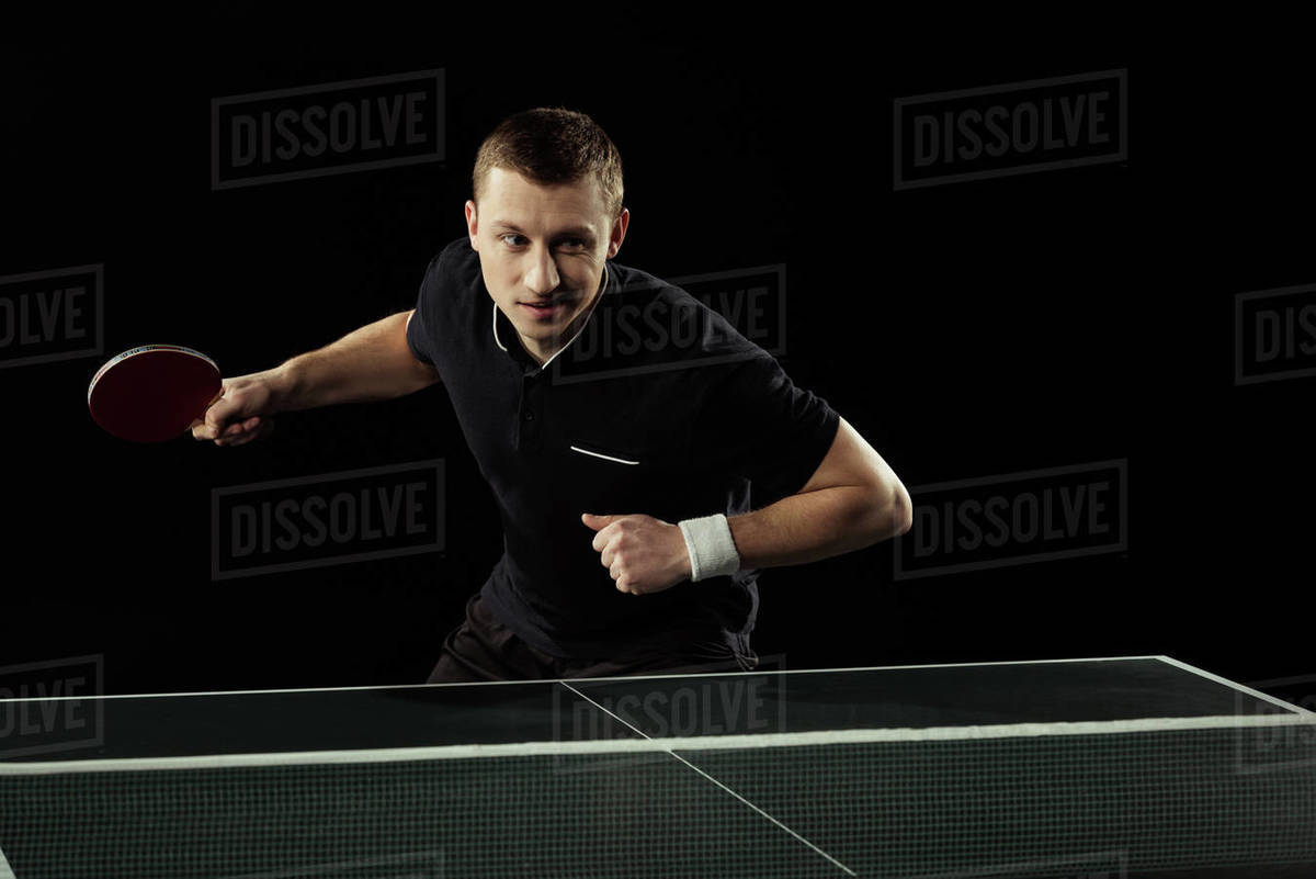 Portrait of young tennis player playing table tennis isolated on black ...