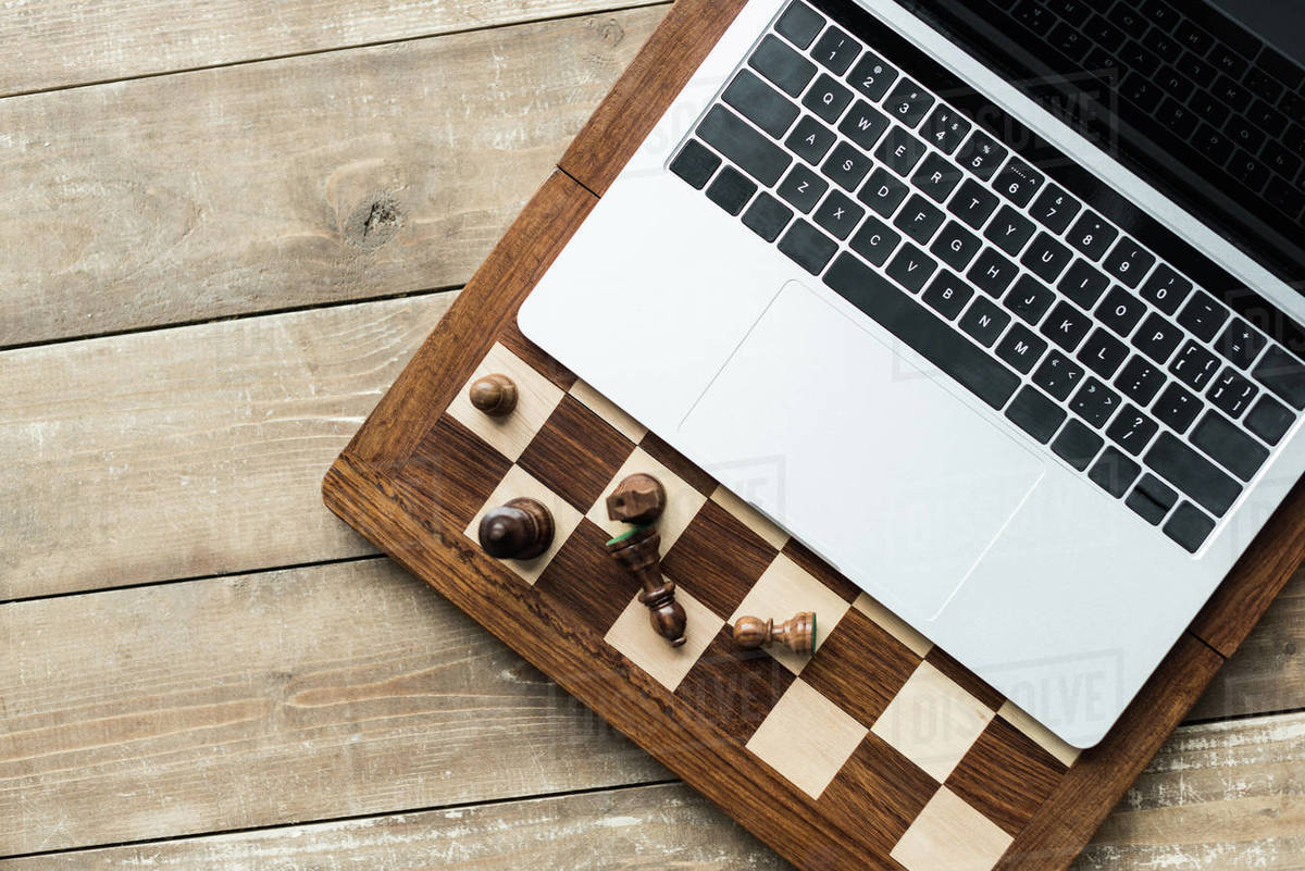 Top view of chess board, laptop and chess pieces on rustic wooden ...