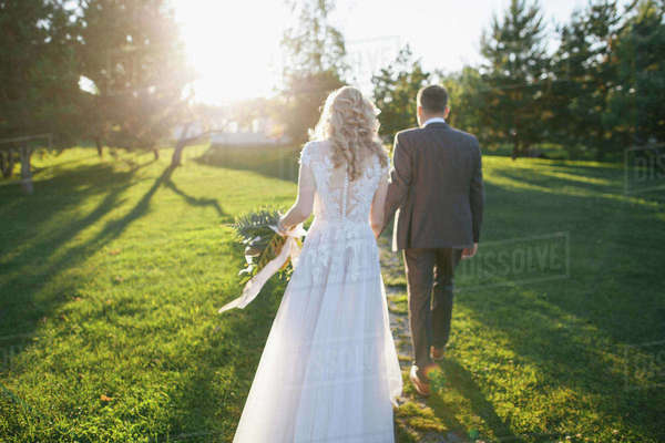 back view of beautiful wedding couple holding hands and walking ...