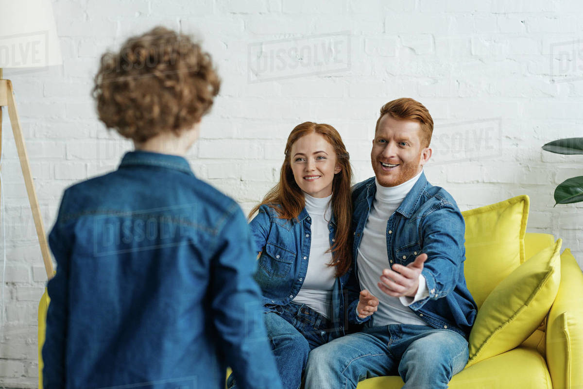 Smiling parents sitting on sofa and calling little son - Royalty-free ...