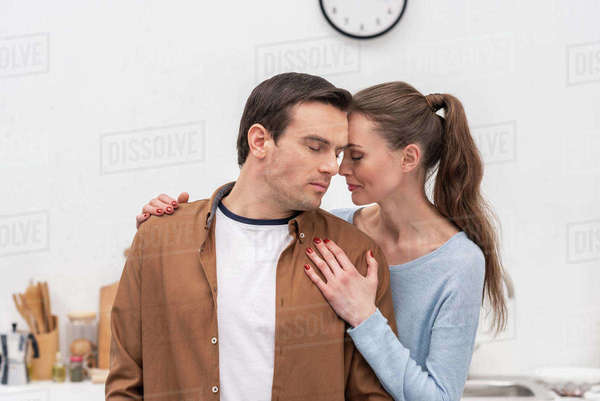 Beautiful adult couple embracing at home in front of white brick wall ...