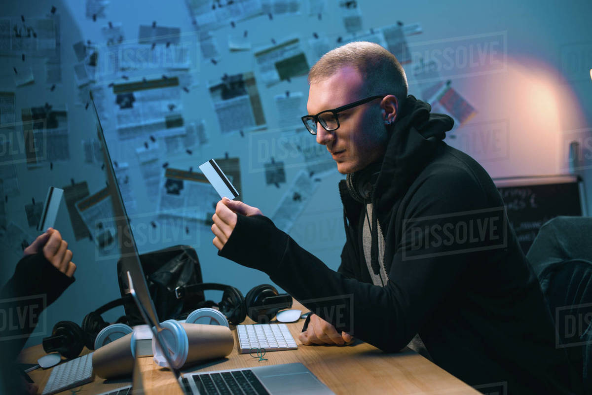 Young hacker holding stolen credit card in dark room - Royalty-free ...