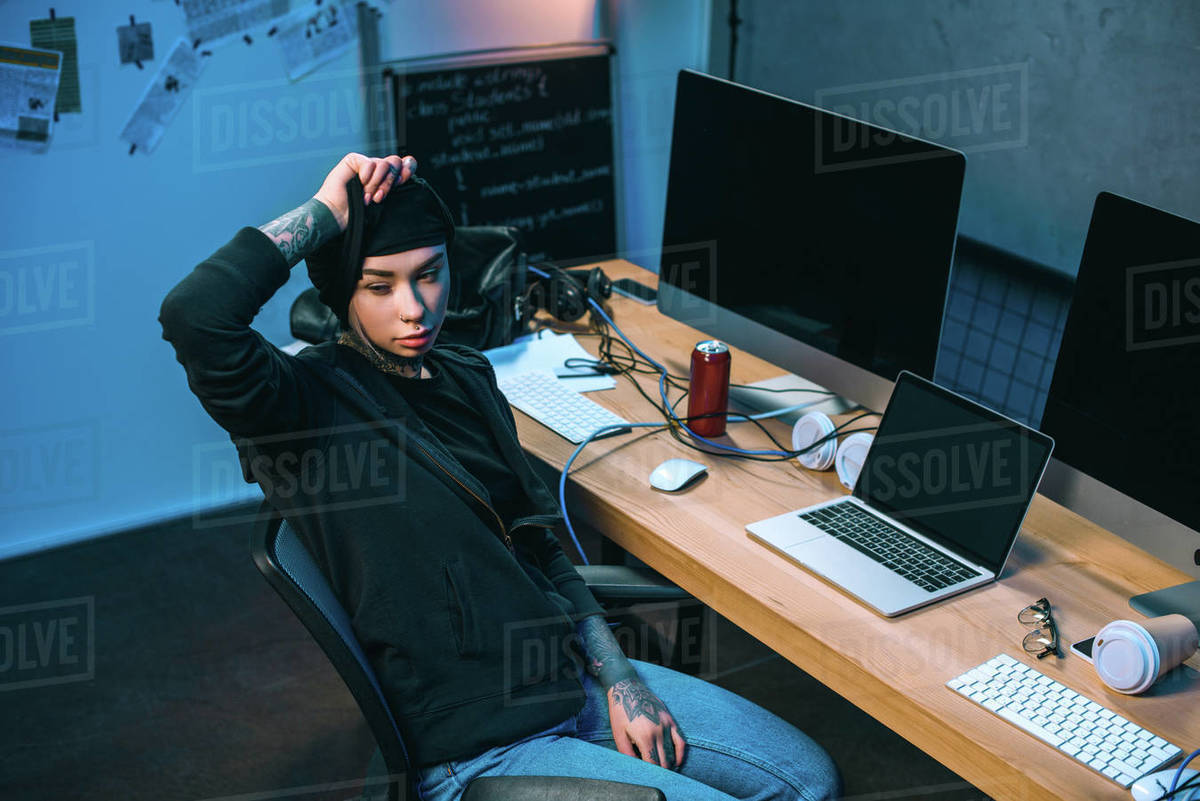 Young female hacker at in front of desk taking off mask - Royalty-free ...